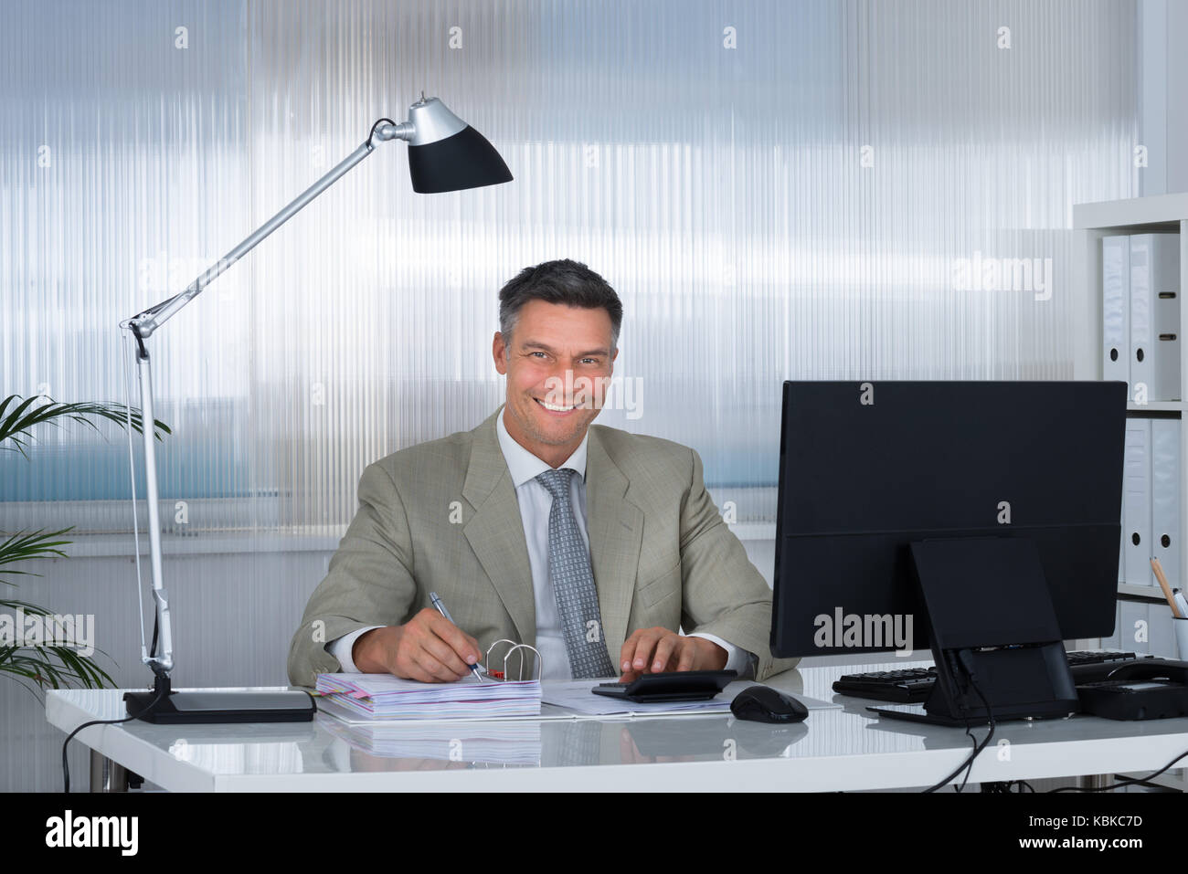 Portrait of smiling accountant using calculator while writing on ...