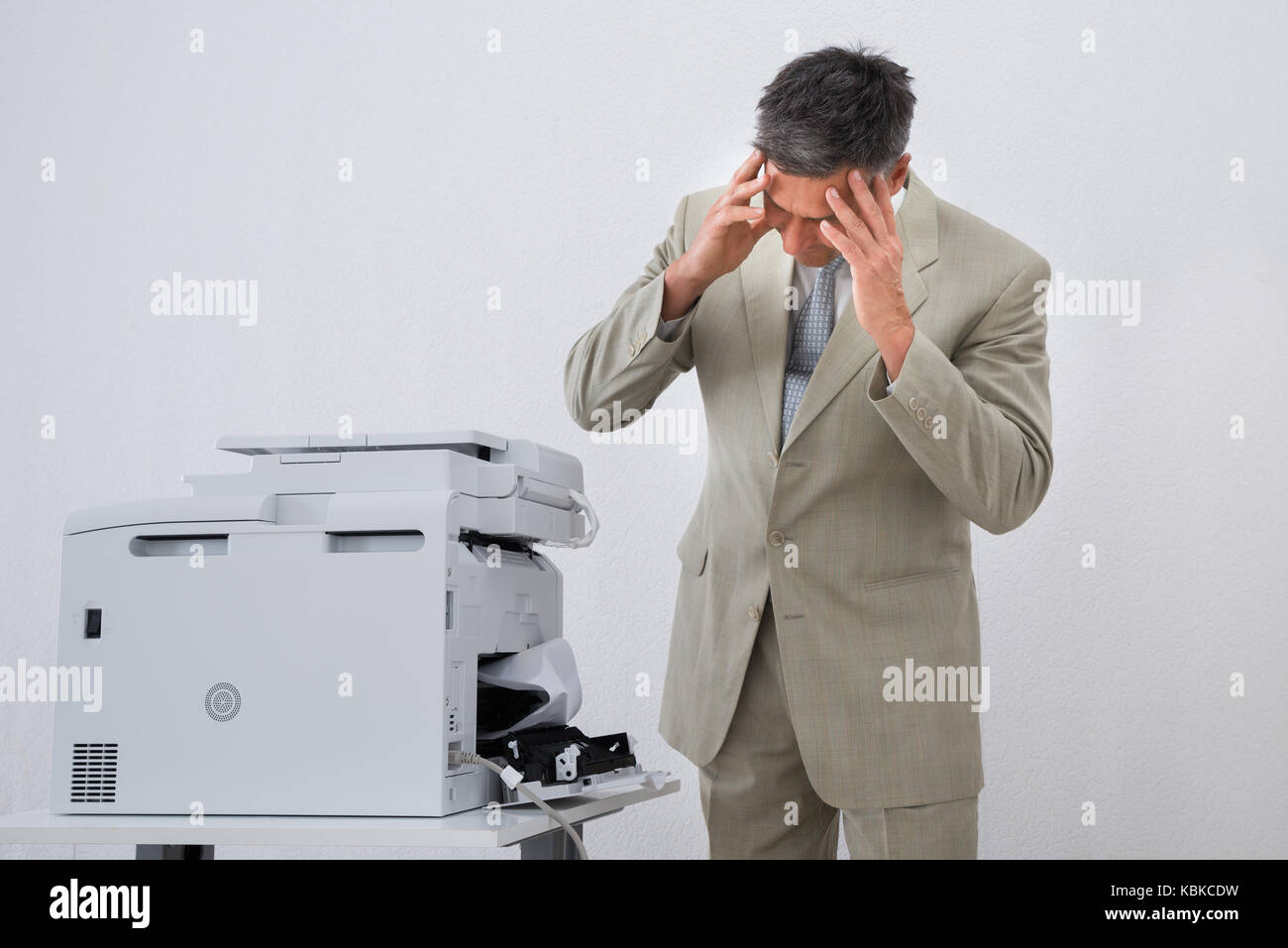 Irritated businessman looking at paper stuck in printer at office Stock ...