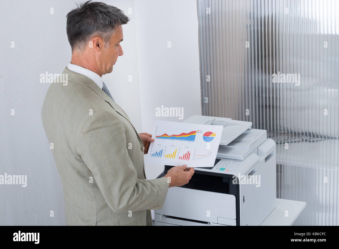 Side view of businessman looking at paper with graphs while standing by ...