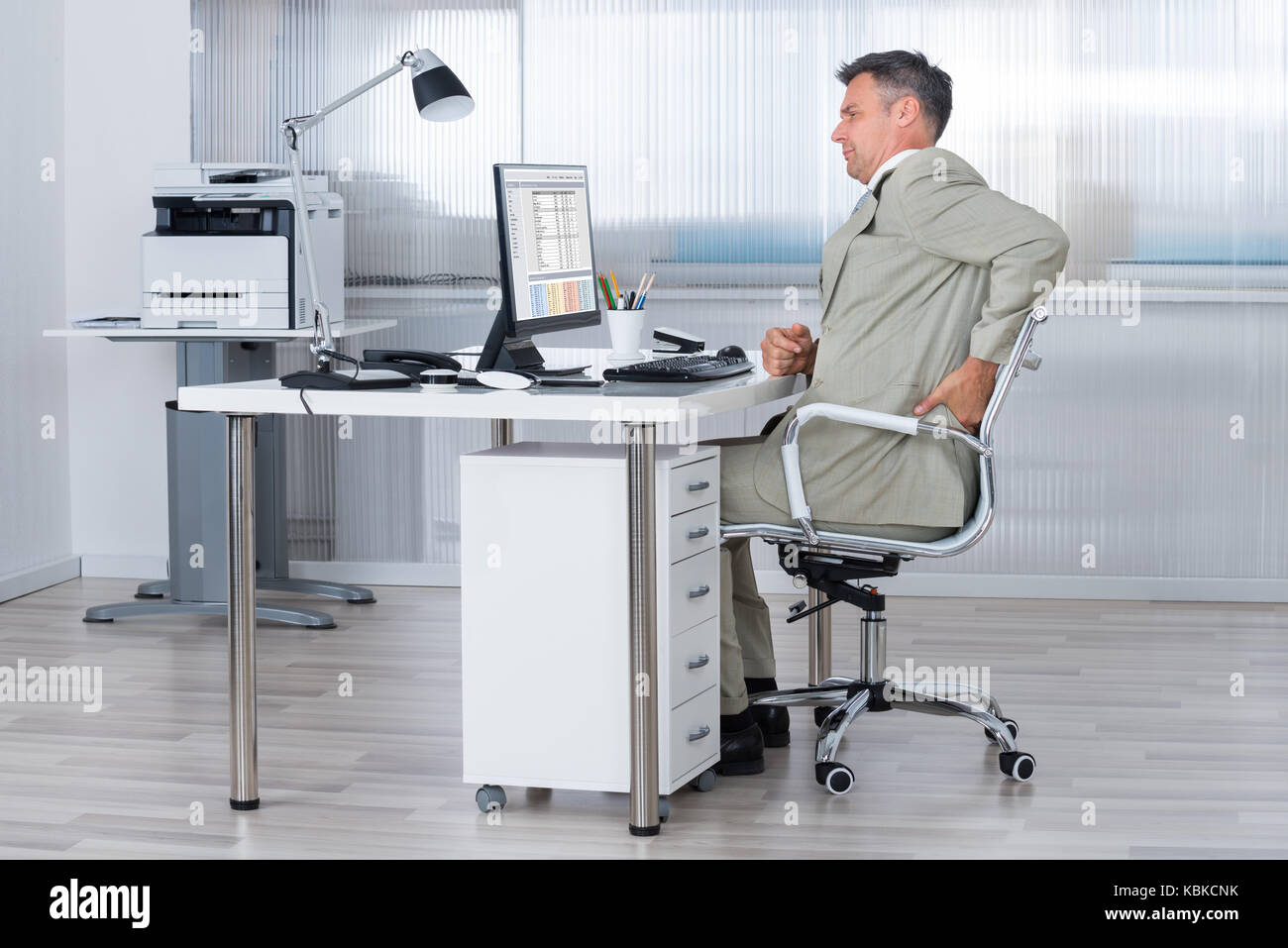 Side view of accountant suffering from back pain at desk in office ...