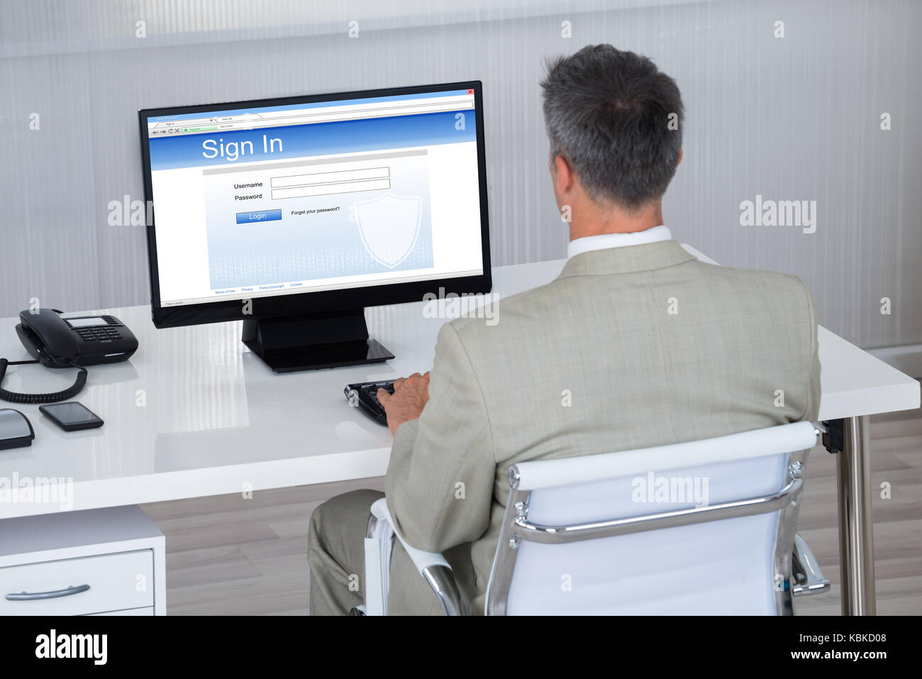 Rear view of businessman signing into website at desk in office Stock ...