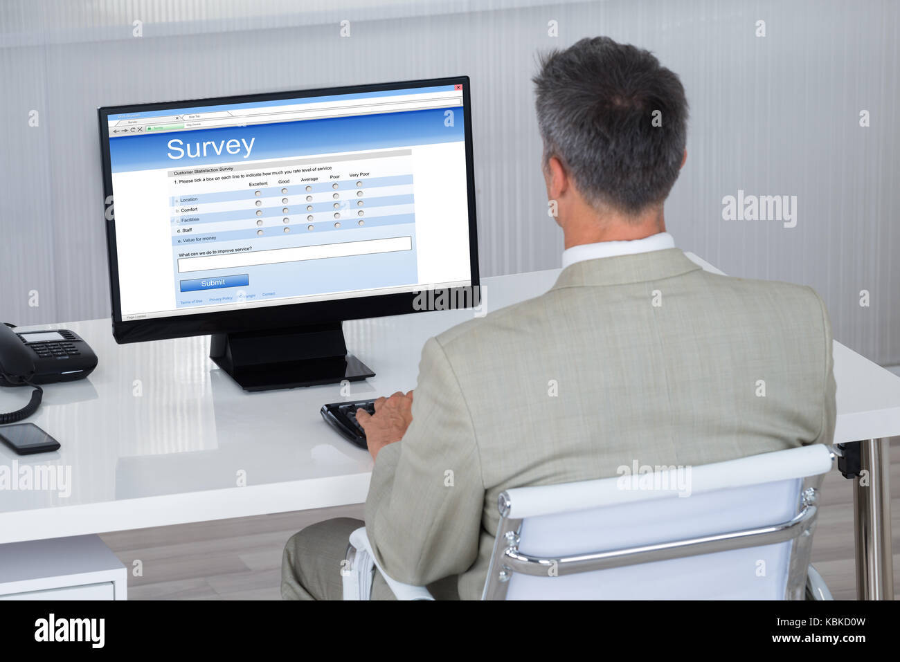 Rear view of businessman filling survey form on computer at desk in ...