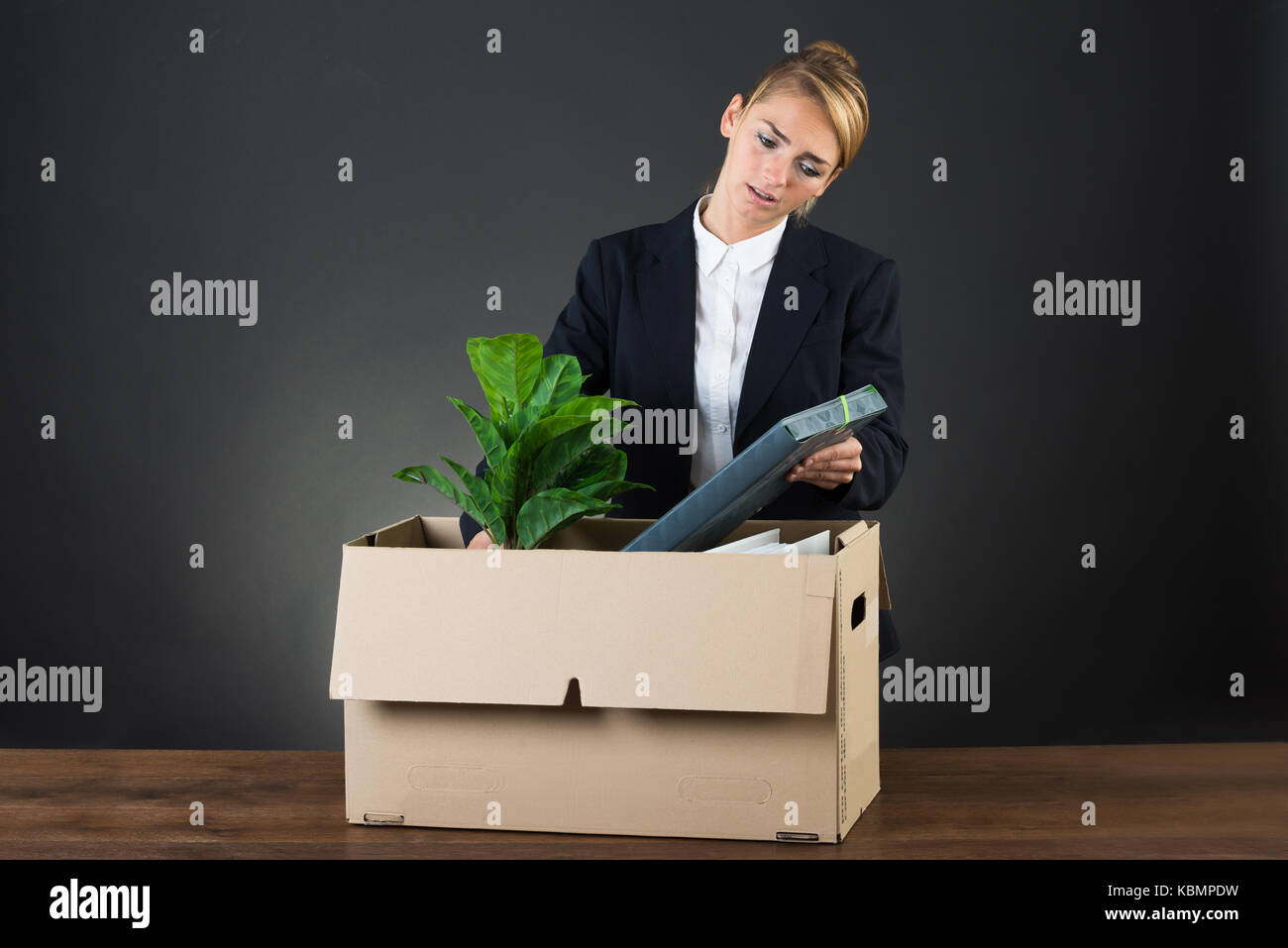 Sad young businesswoman packing her belongings at desk over gray ...