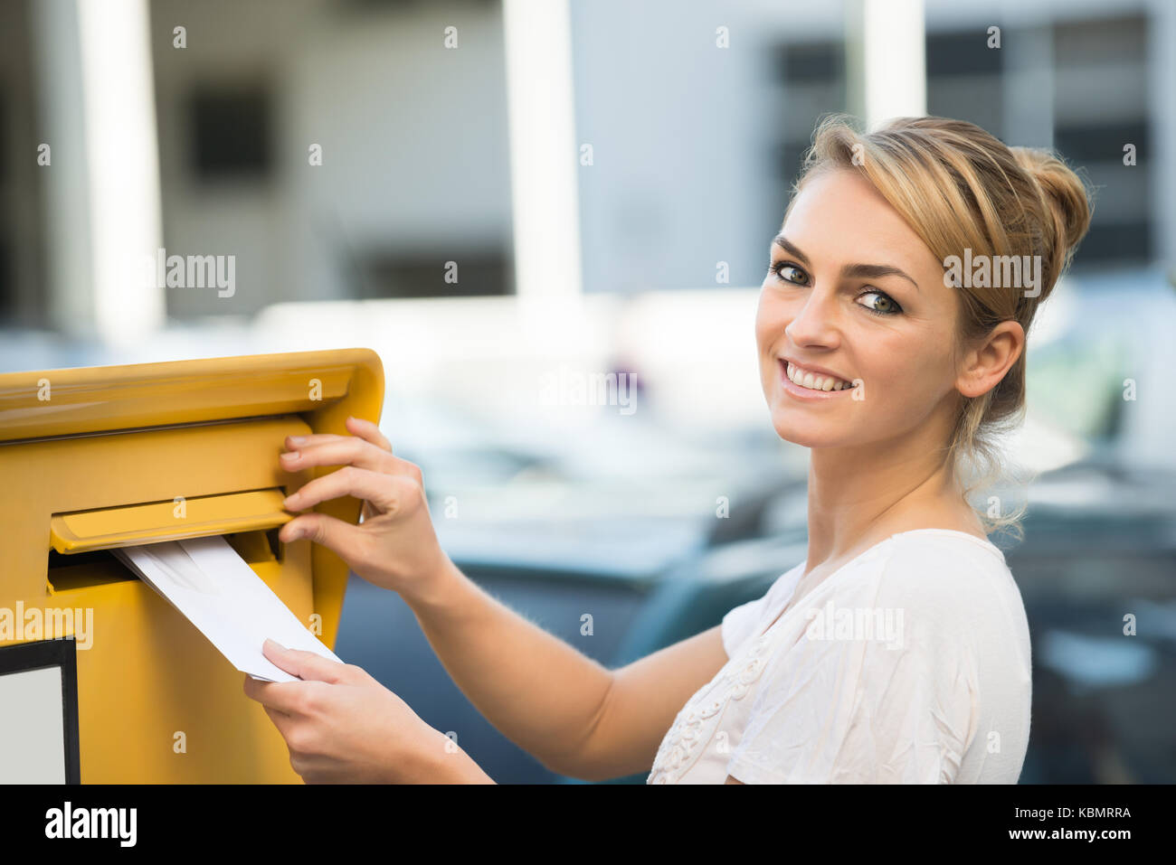 Happy young woman inserting letter in mailbox Stock Photo - Alamy