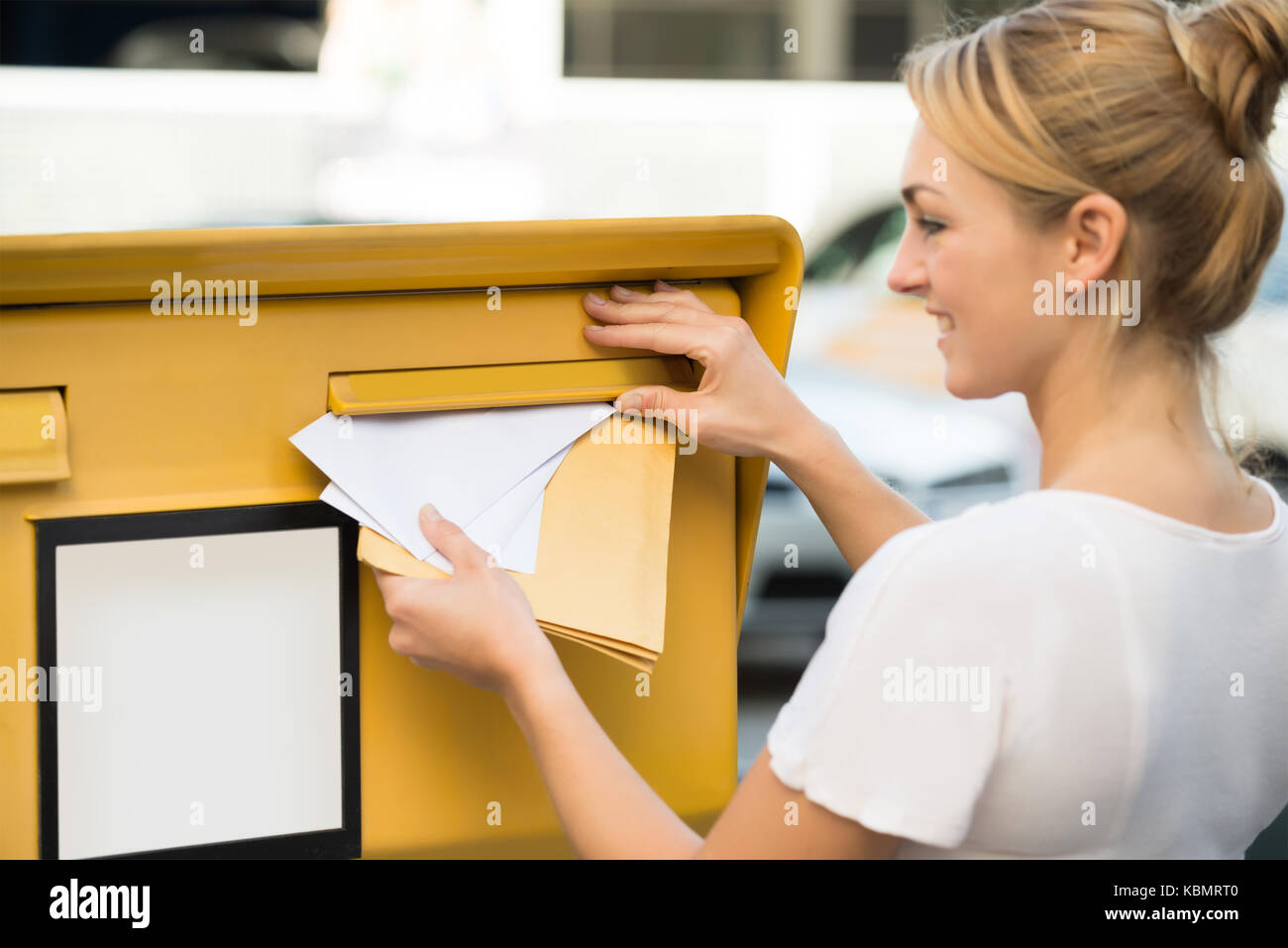 Happy young woman inserting letter in mailbox Stock Photo - Alamy