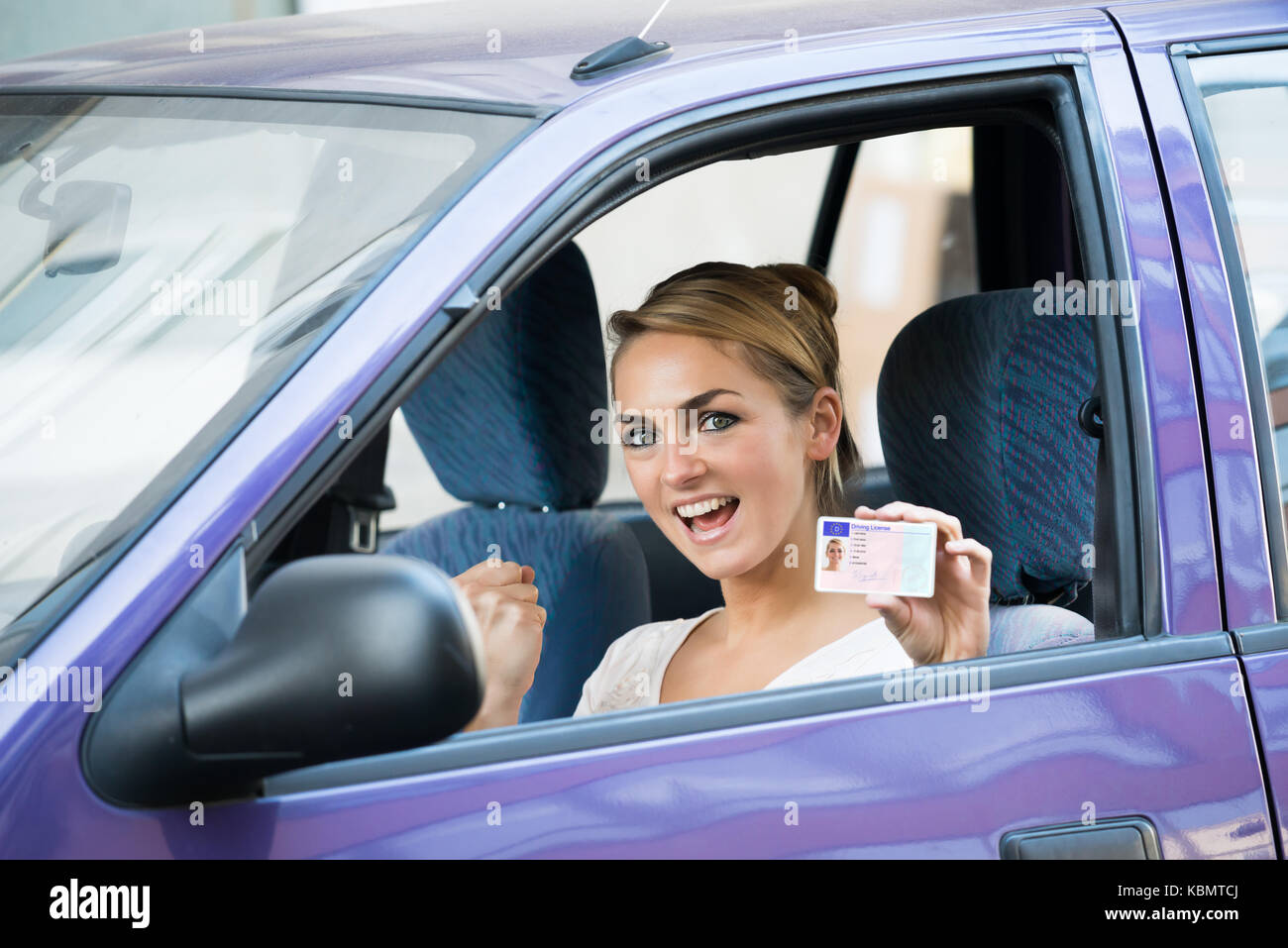 Portrait of excited young woman showing license while sitting in car ...