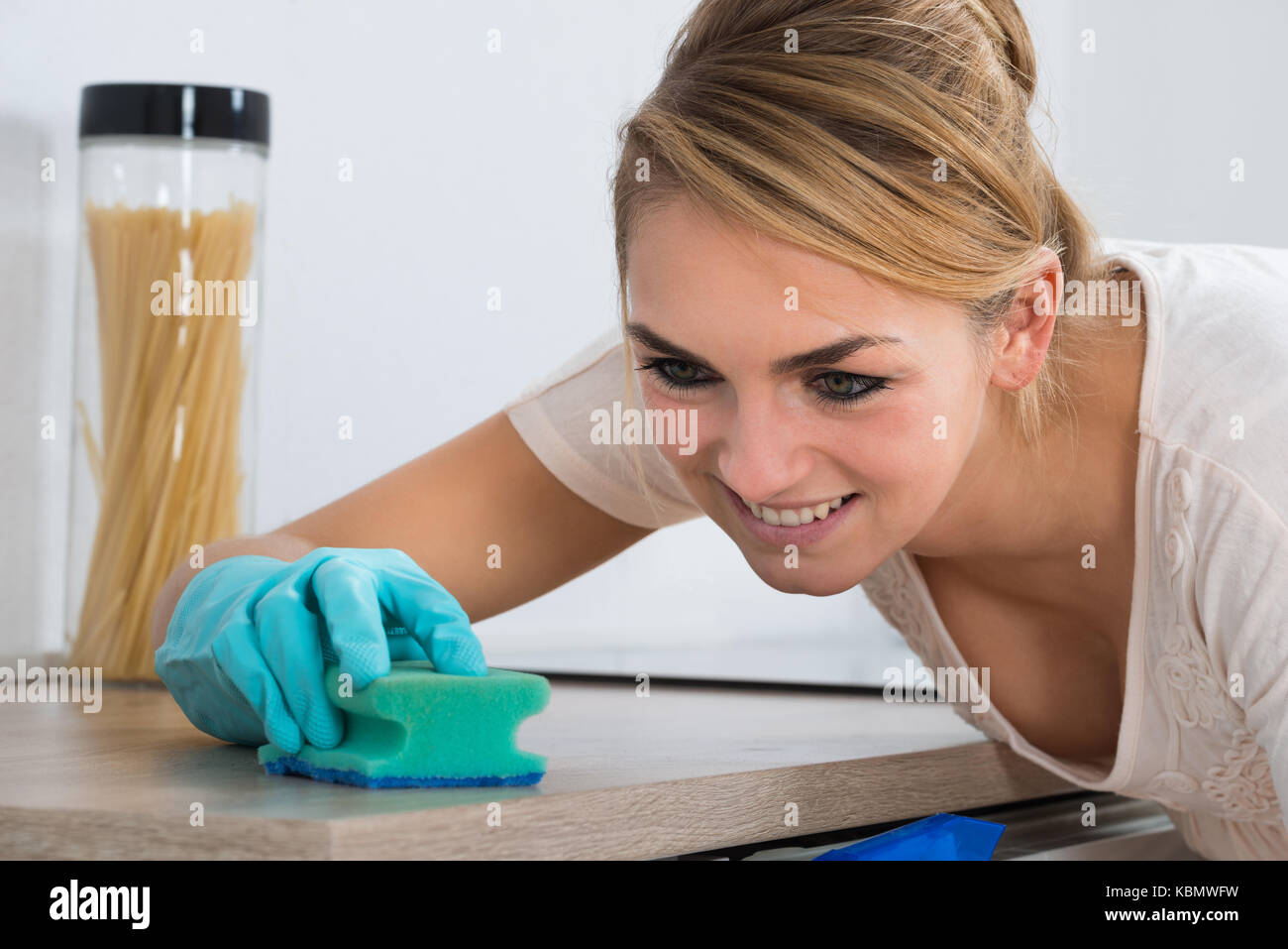 Young woman cleaning kitchen counter with sponge at home Stock Photo ...