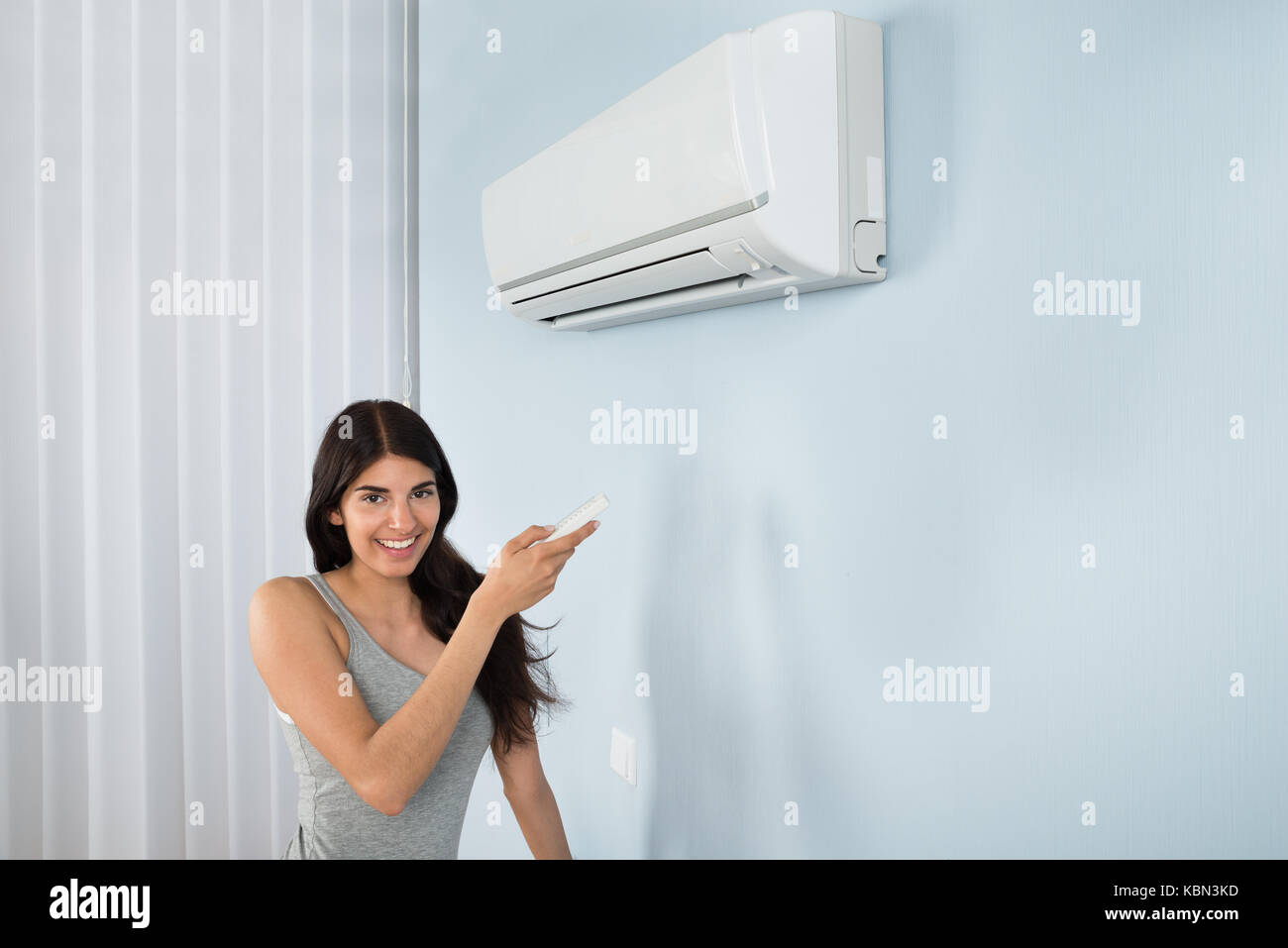 Young Happy Woman Holding Remote Control Air Conditioner In House Stock ...