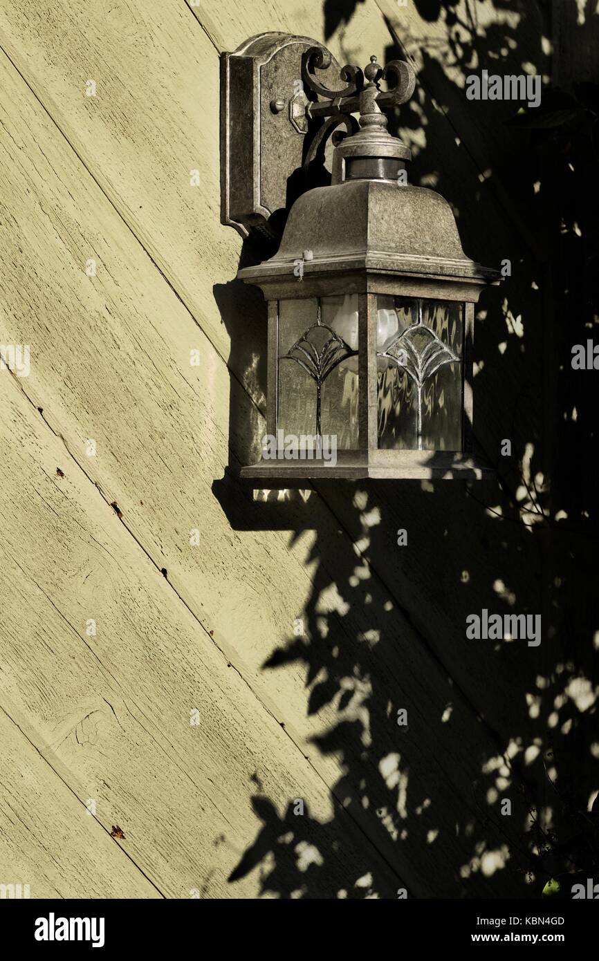 Cedar sided wall and lantern with tree filtered sunlight casting late ...