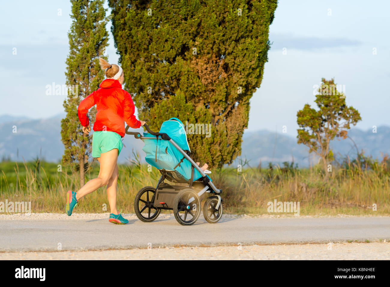 Running mother with child in stroller enjoying motherhood at sunset and ...