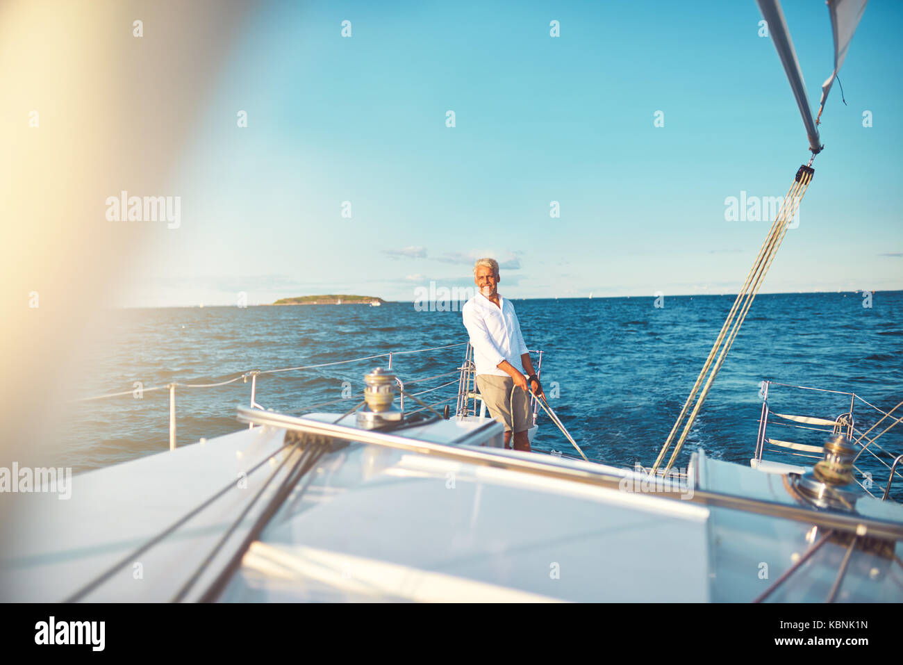 Smiling mature man standing alone on the deck of his boat steering with ...