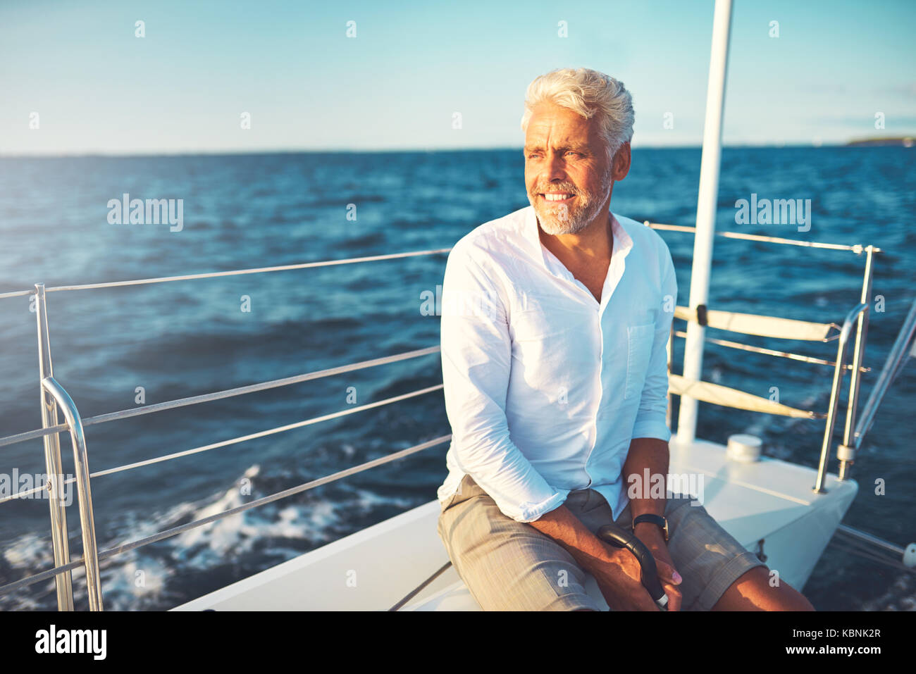 Smiling mature man sitting alone on the deck of his boat enjoying a ...