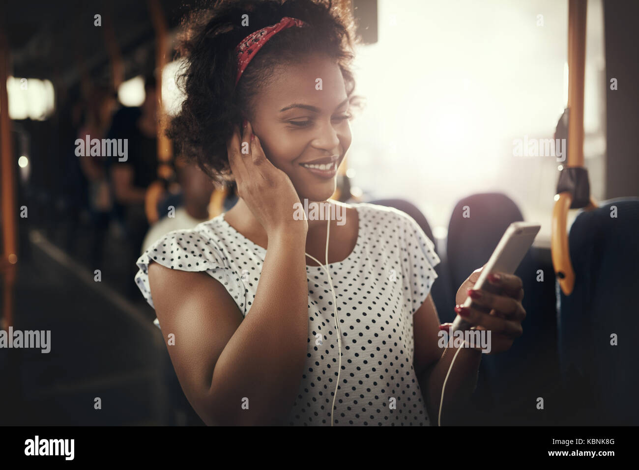 Young African woman smiling while standing on a bus listening to music ...