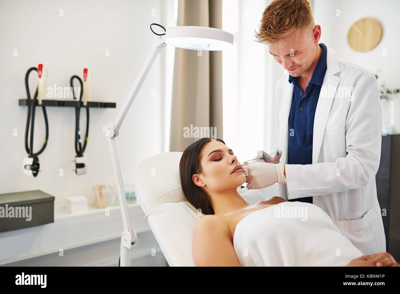 Young male doctor focused on performing a botox injection to the cheek ...