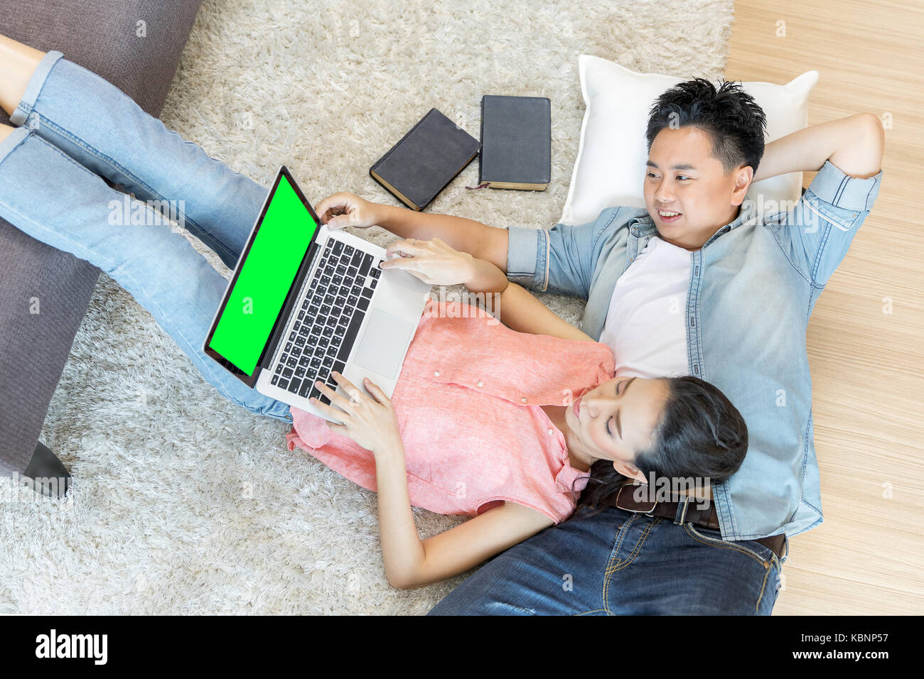 Young Asian Couples lying down and using laptop together in living room of contemporary house ...