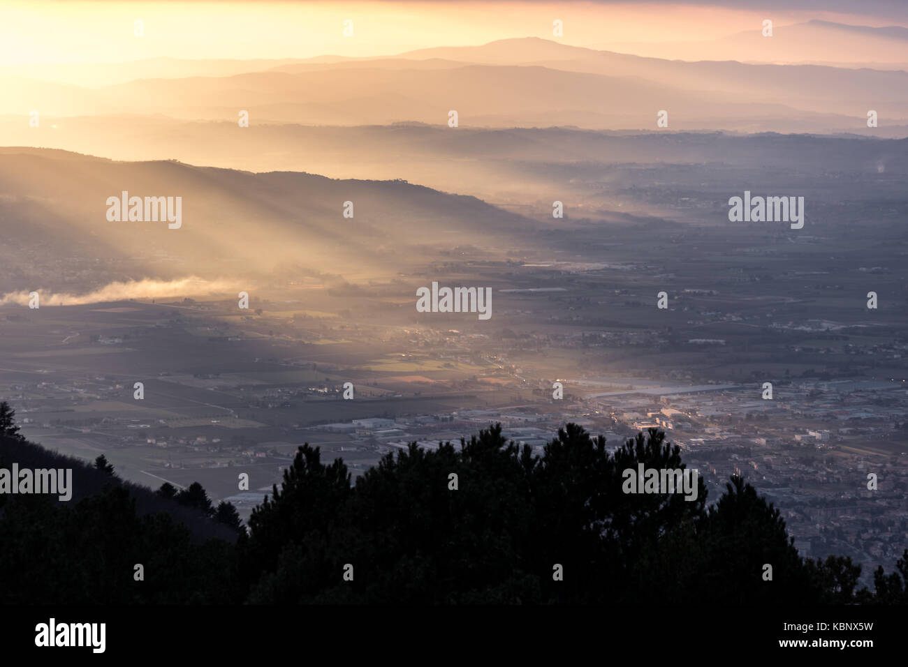 Aerial view of a valley, with sun rays coming out behind some mountains ...