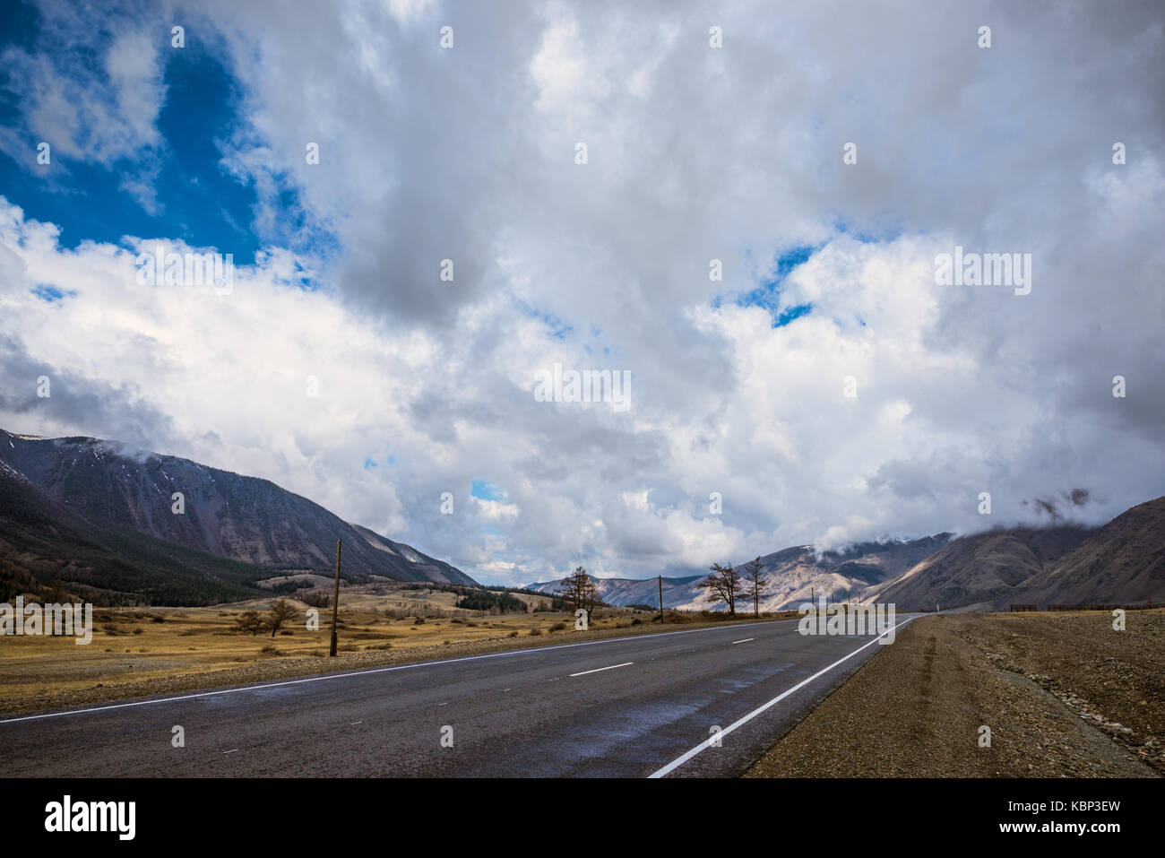 panoramic view of plain with road at root of mountains and fluffy ...