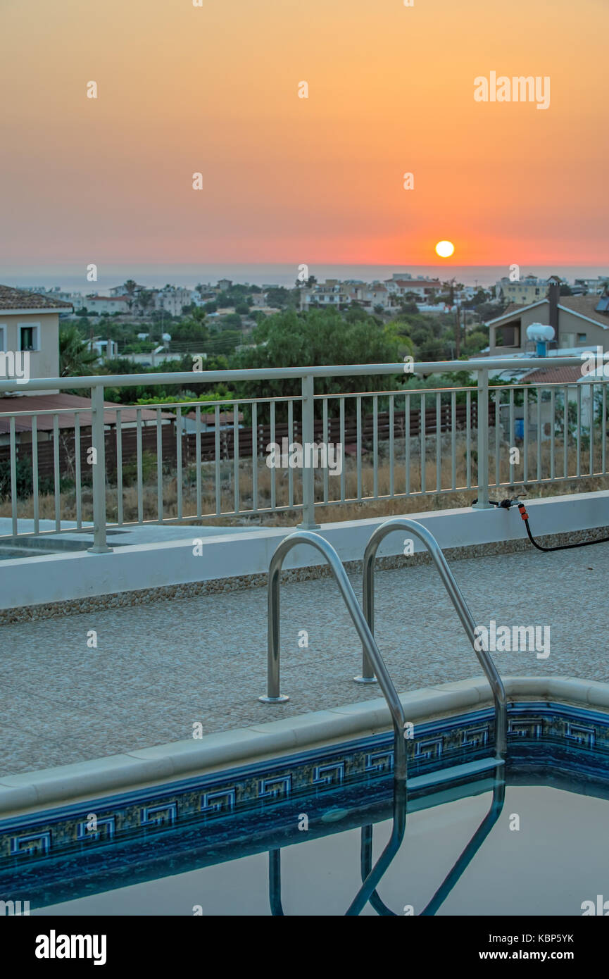 Swimming pool and sunset over village and sea on horizon Stock Photo ...