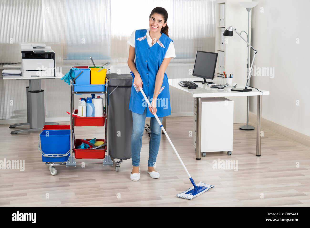 Full length portrait of happy female janitor mopping floor in office ...