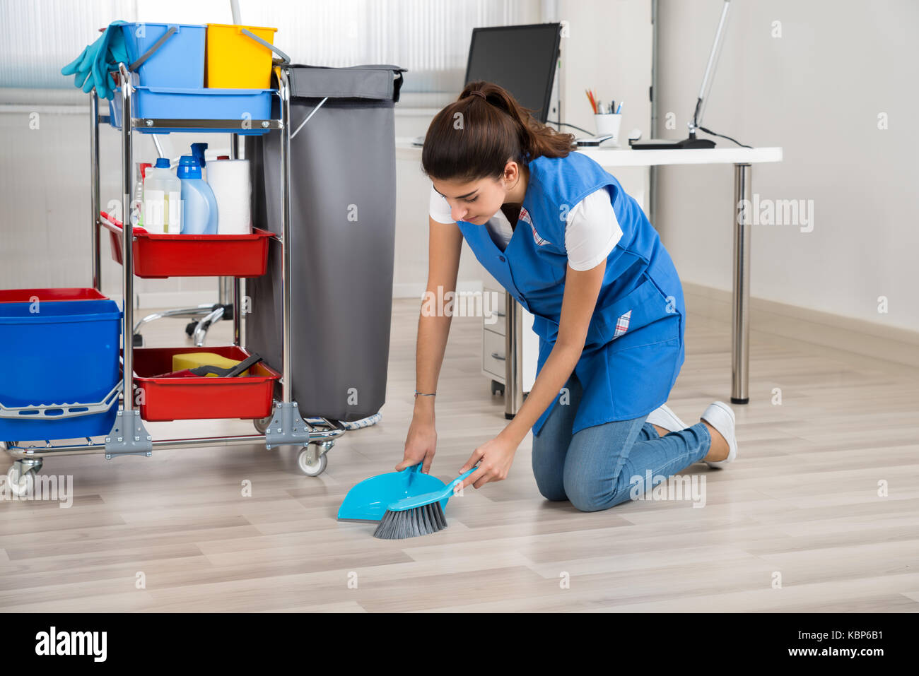 Full length of young female cleaner sweeping wooden floor in office ...