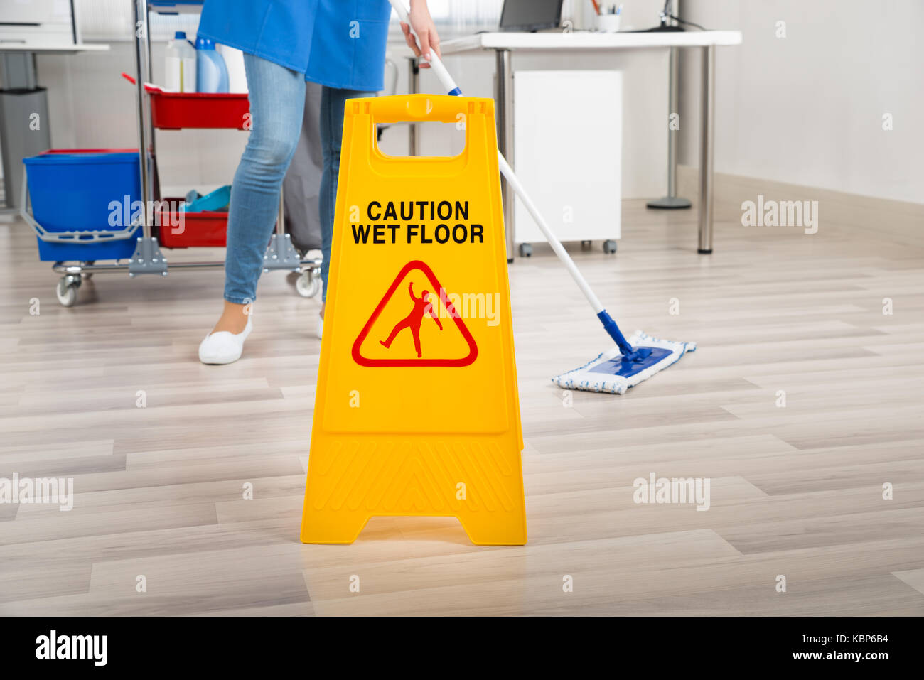 Low section of female janitor mopping floor by yellow wet caution sign ...