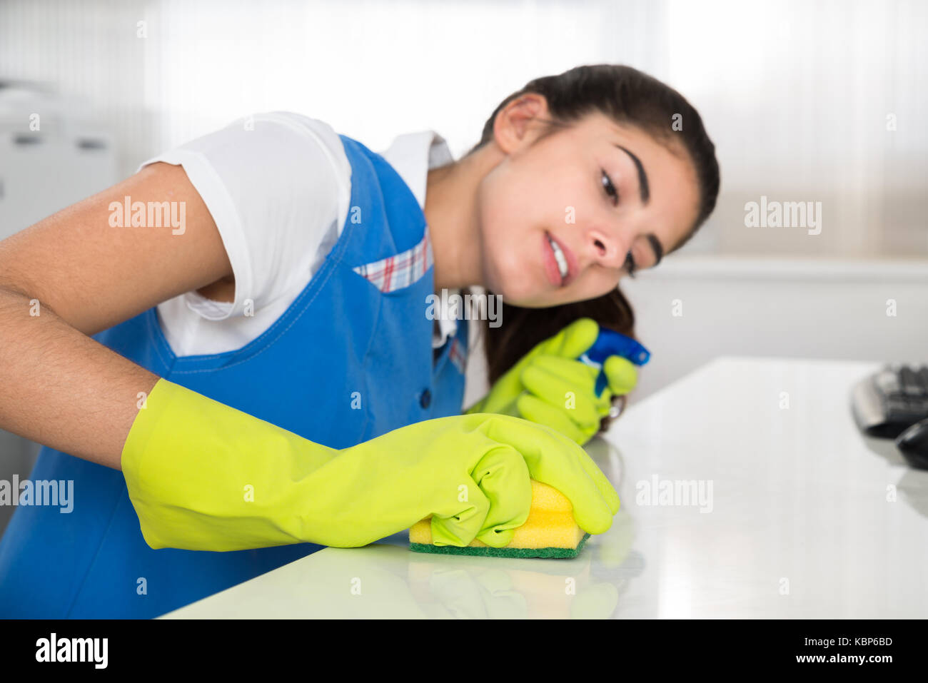 Young female janitor cleaning desk with sponge at office Stock Photo ...