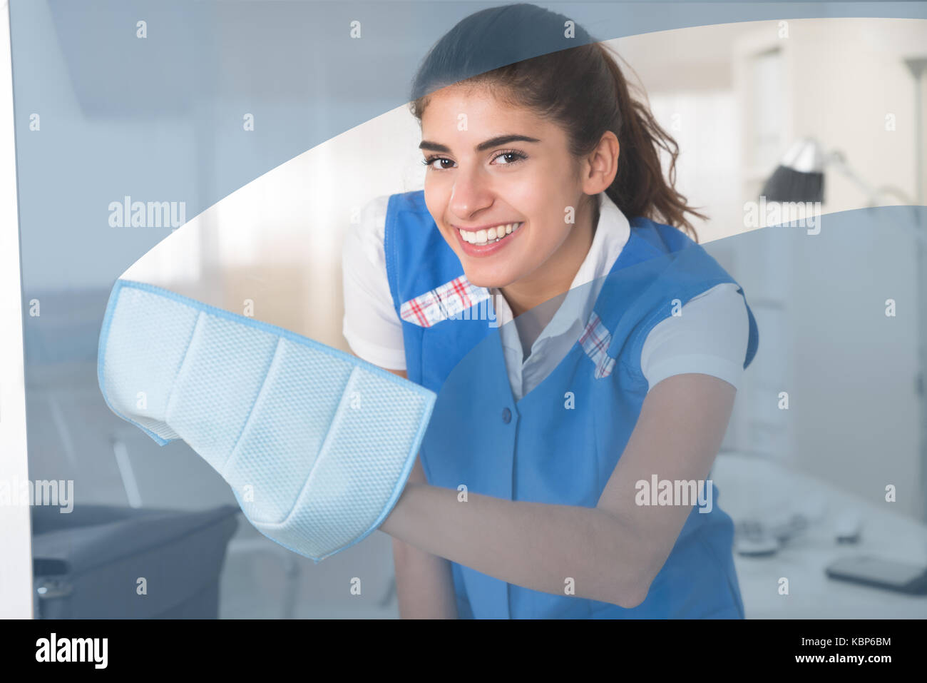 Portrait of happy young female worker cleaning glass window with rag at ...