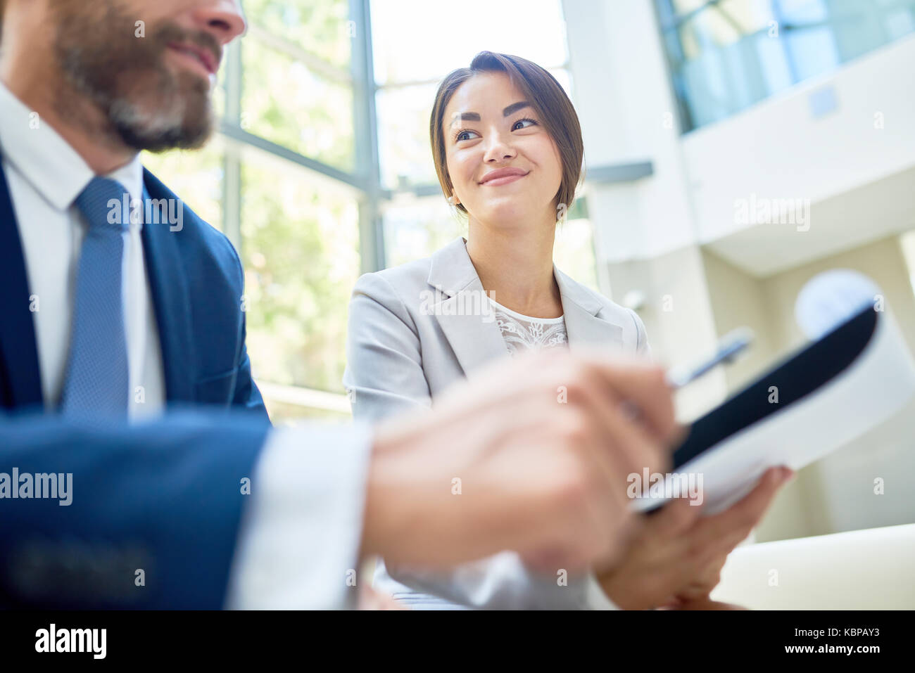 Portrait of pretty young manager looking at male colleague with ...