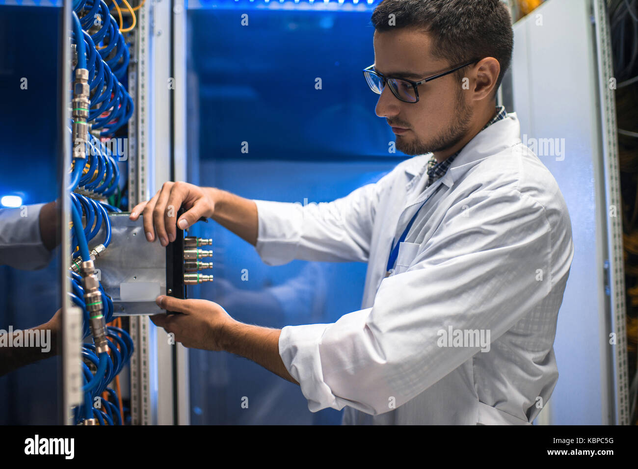 Side view portrait of young man in lab coat taking out blade server ...