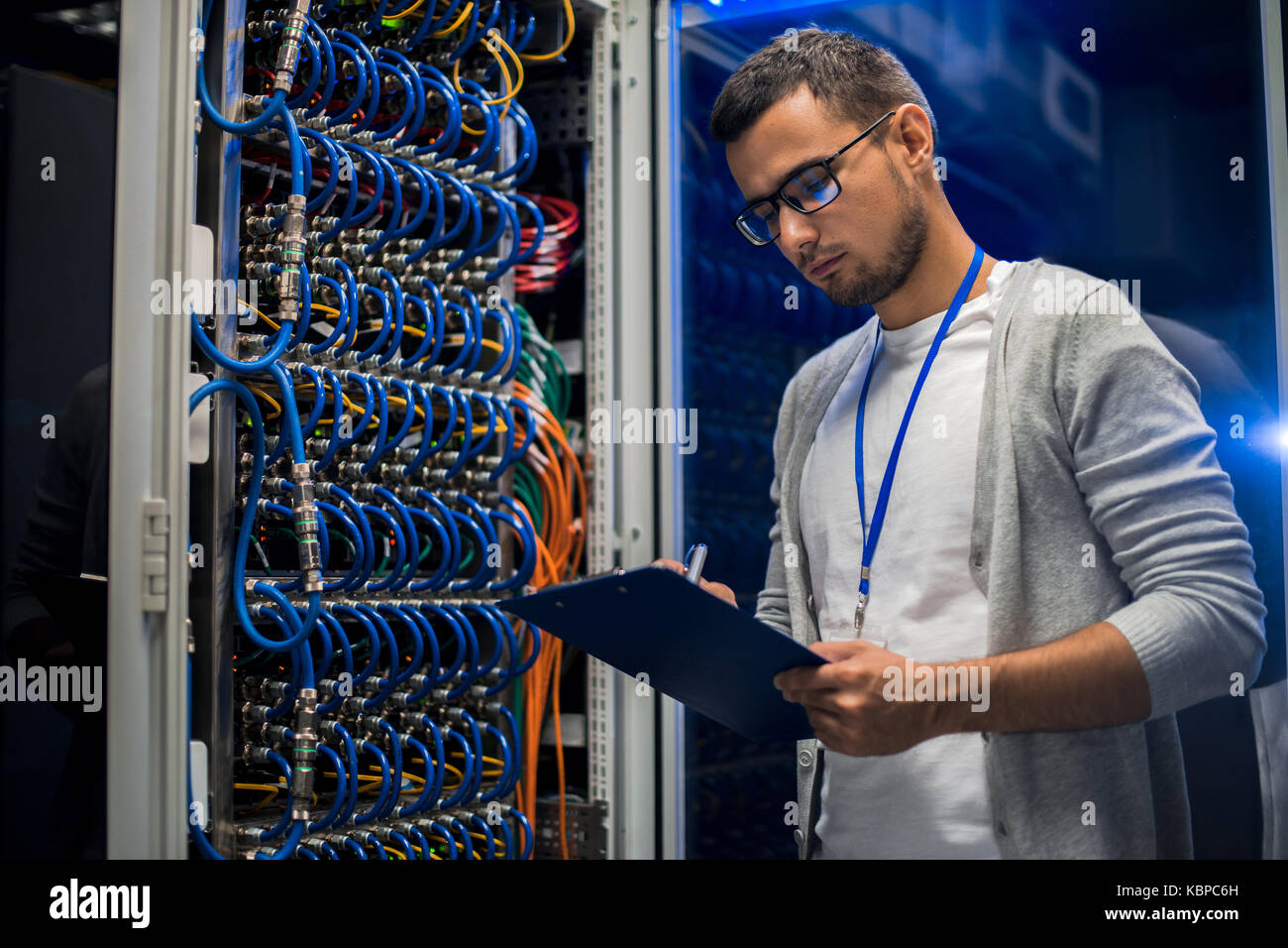 Portrait of young network engineer standing by server cabinet while ...