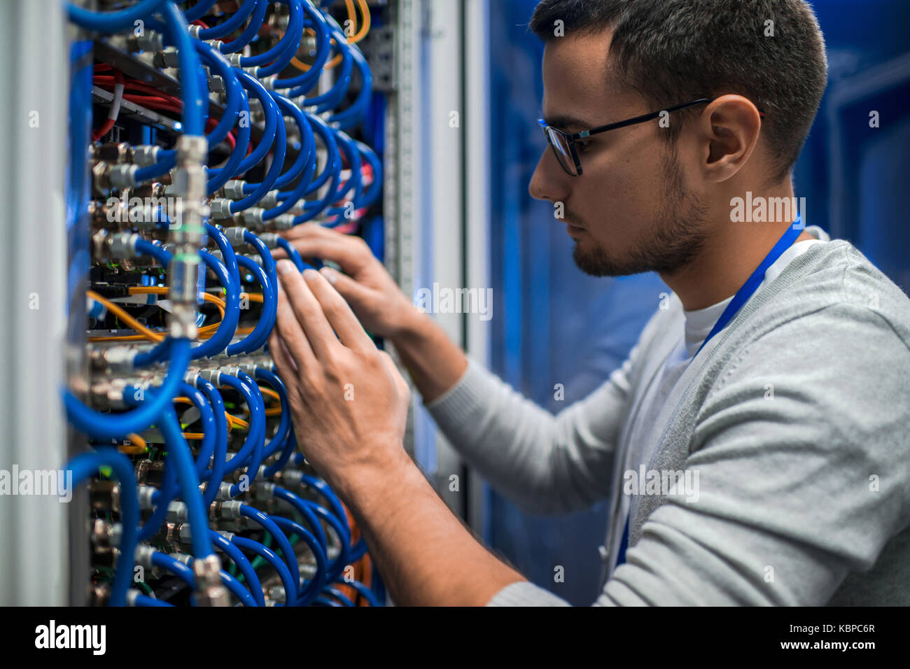 Side view portrait of young man connecting wires in server cabinet ...