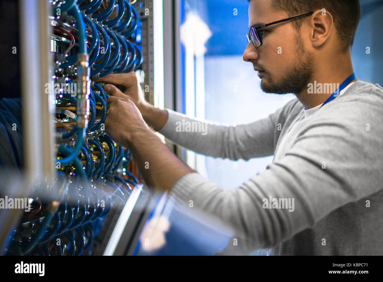 Side view portrait of young man wearing glasses connecting cables in ...