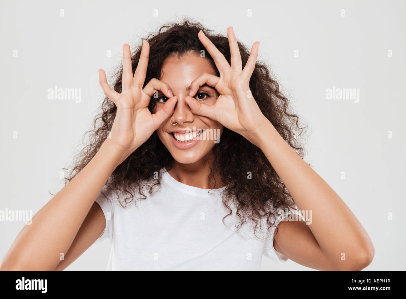 Smiling curly woman holding hands on face and showing ok signs over ...