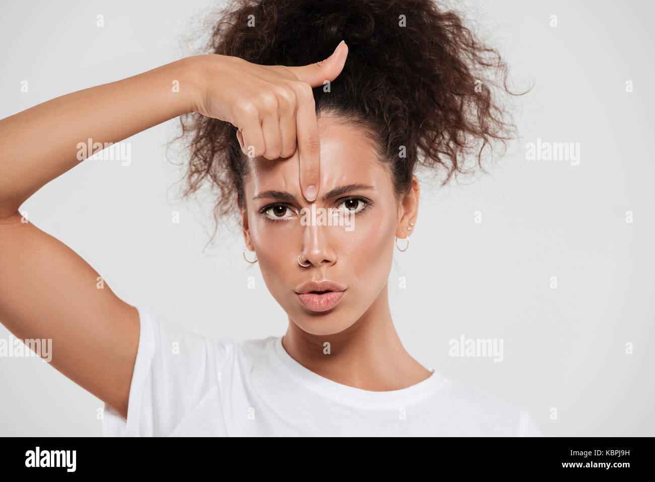 Pretty young woman with curly hair with forefinger on her forehead ...