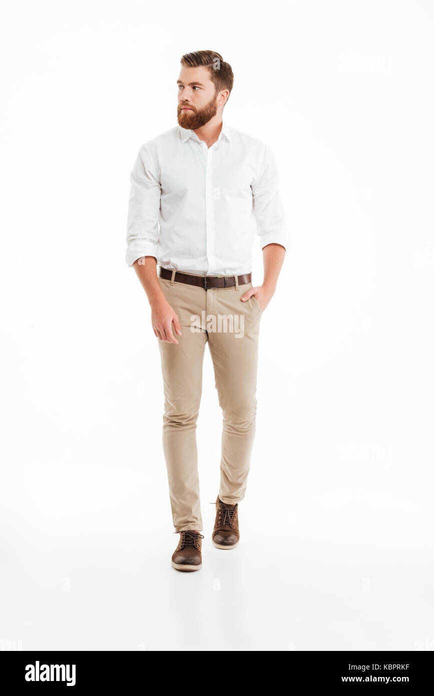 Picture of handsome young bearded man walking over white wall ...