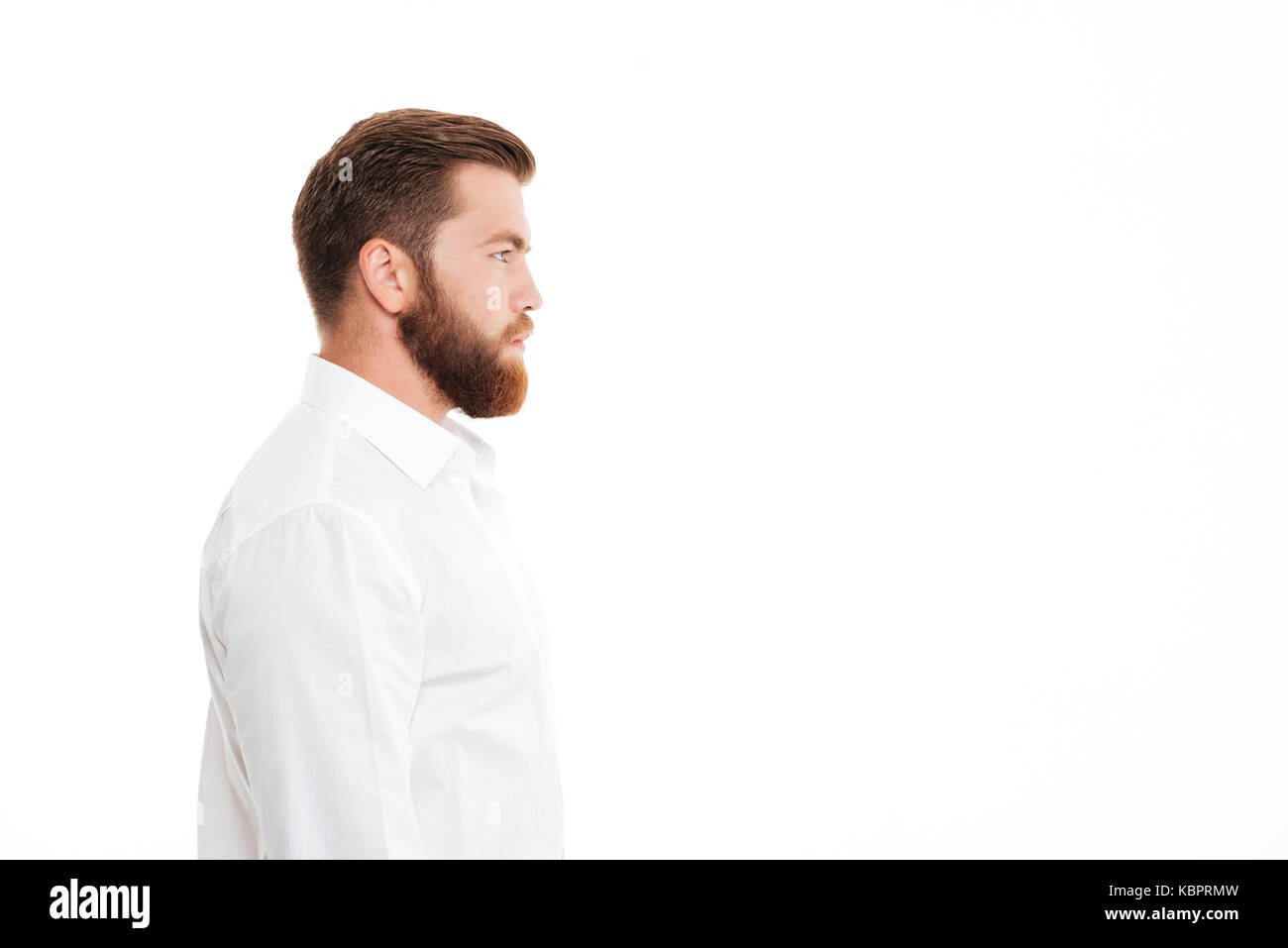 Photo of serious young bearded man standing over white wall background ...