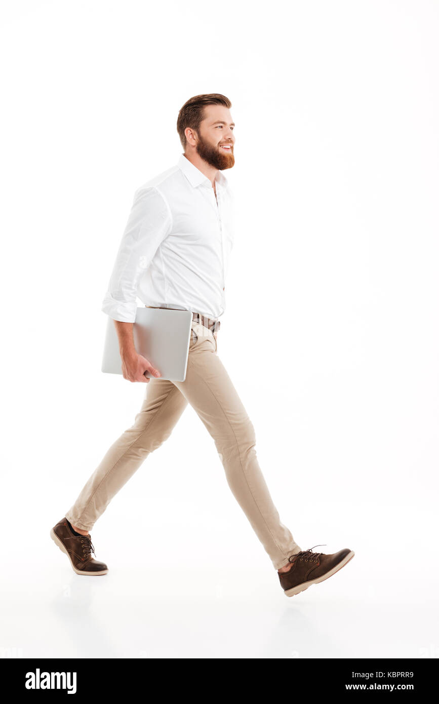Picture of handsome young bearded man walking over white wall ...