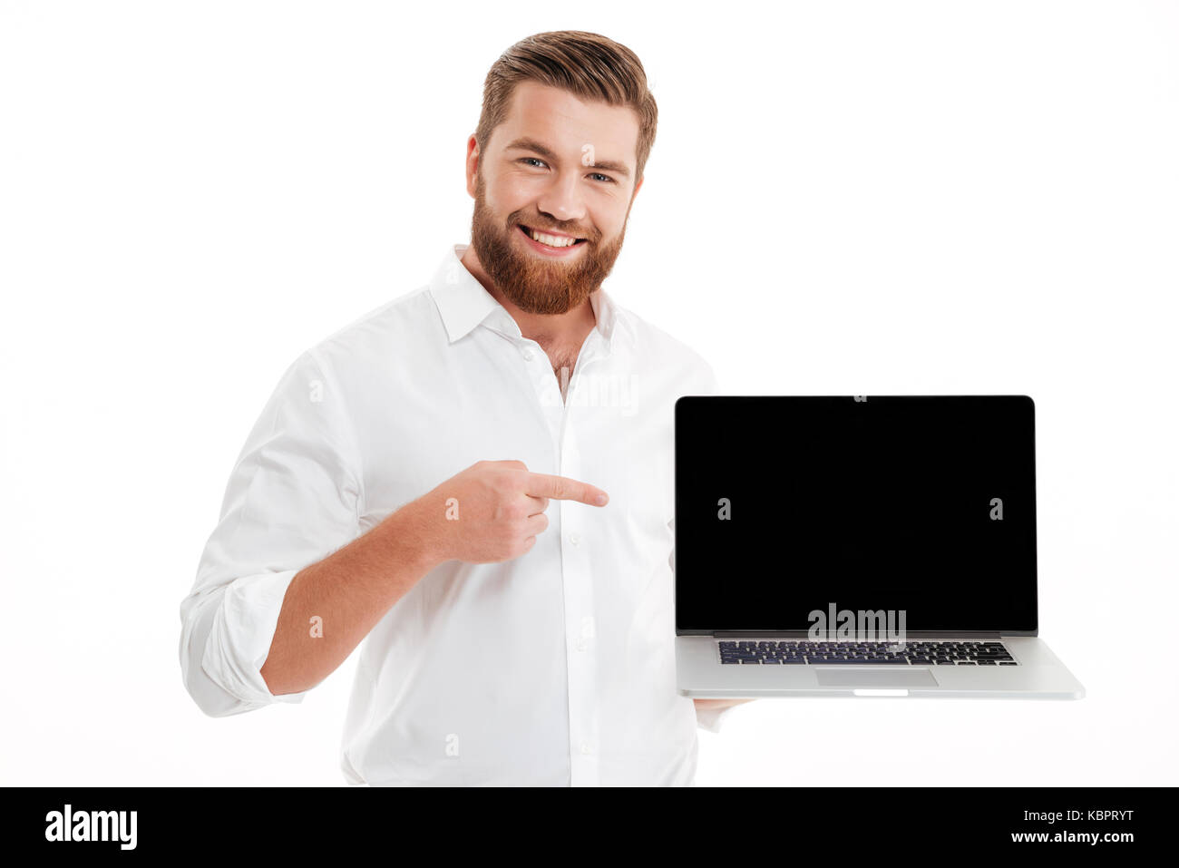 Smiling young bearded man pointing finger at blank screen laptop ...