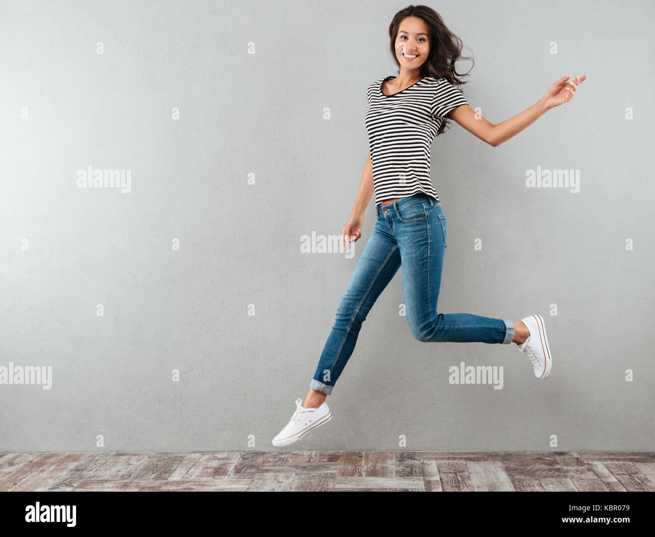 Full length portrait of a cheerful casual asian woman jumping isolated ...