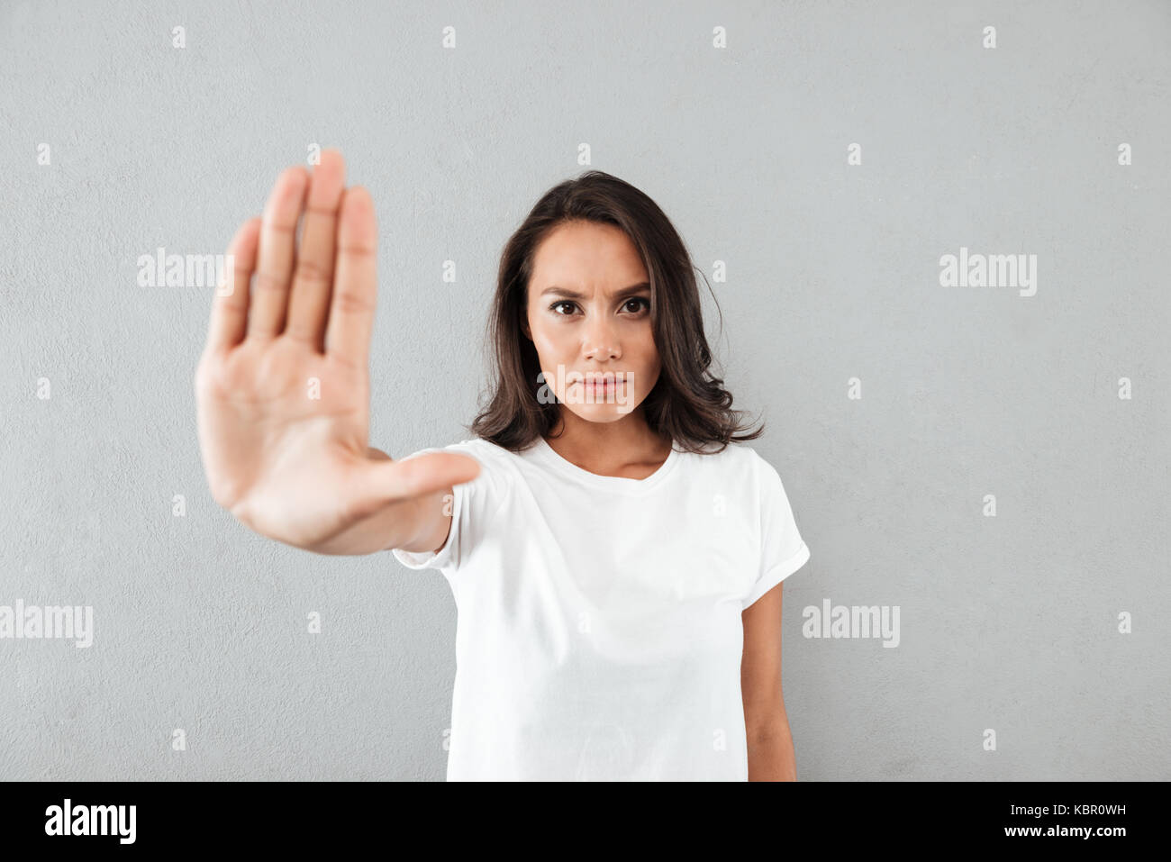Serious young asian woman showing stop gesture with her palm while ...