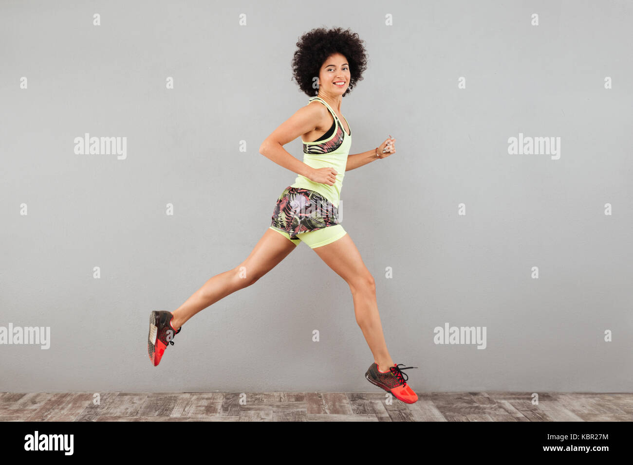 Side view of smiling woman running in studio and looking at the camera ...