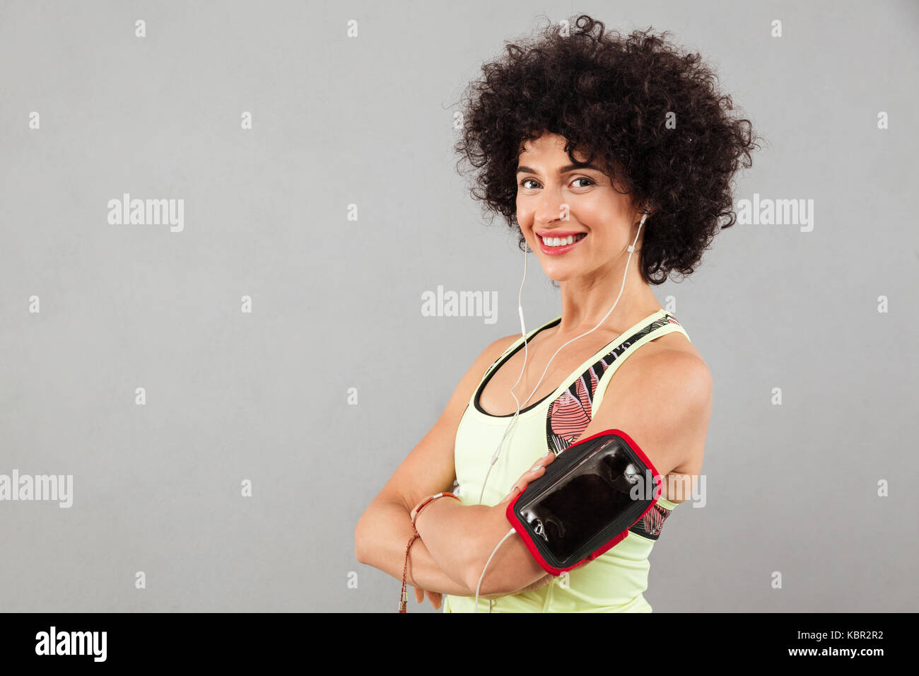 Side view of smiling curly fitness woman standing with crossed arms and ...