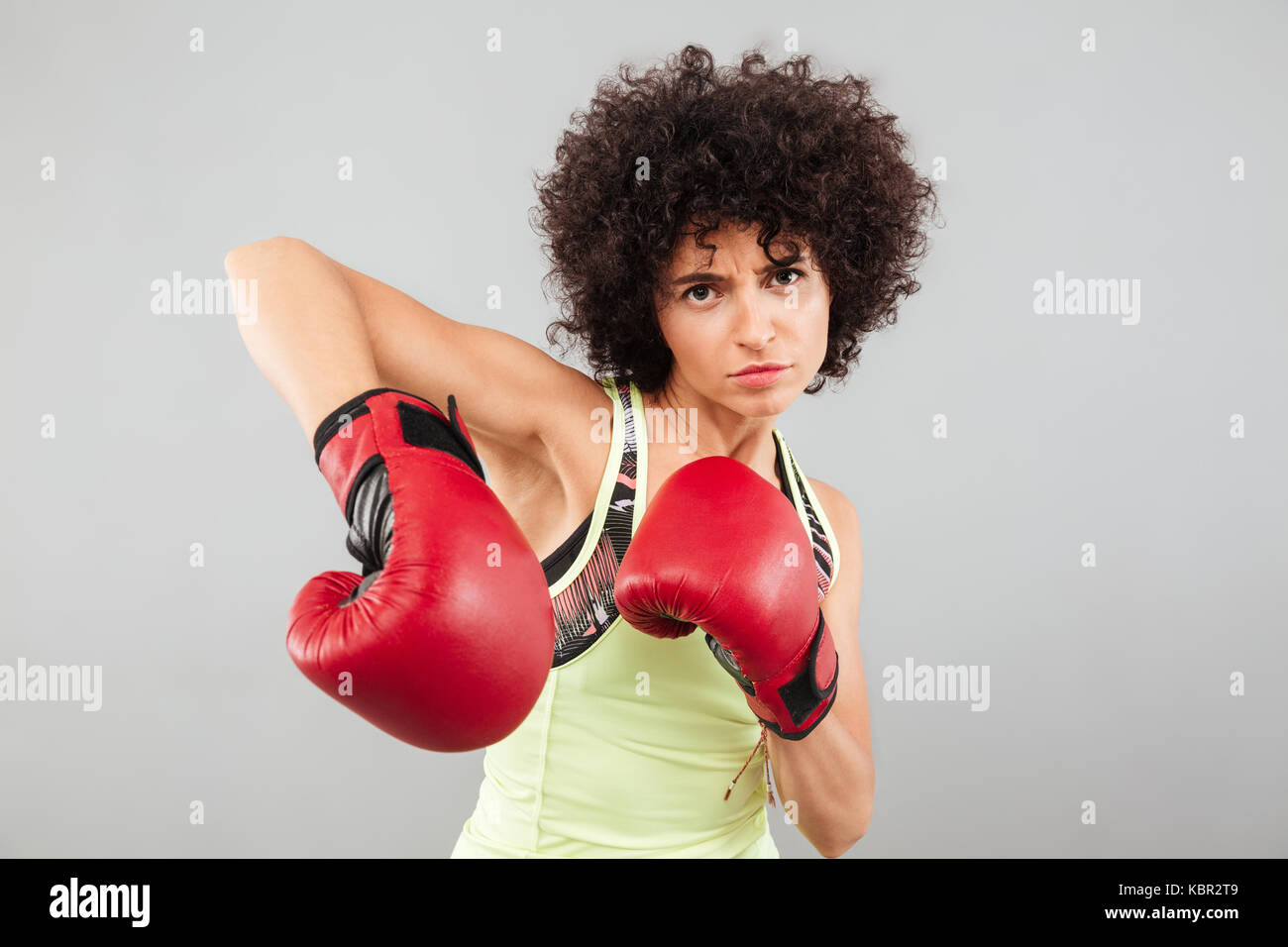 Serious curly sports woman training with boxing gloves over gray ...