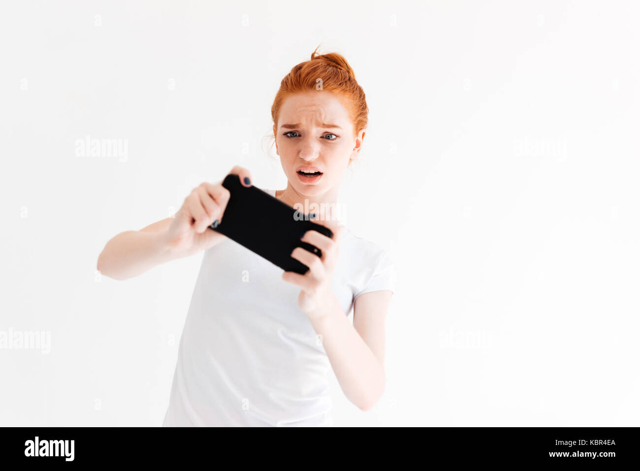 Upset ginger woman in t-shirt playing on her smartphone over white ...