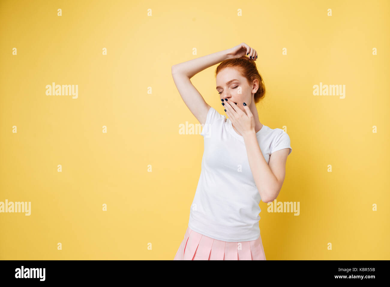 Tired ginger girl covering her mouth with closed eyes over yellow ...