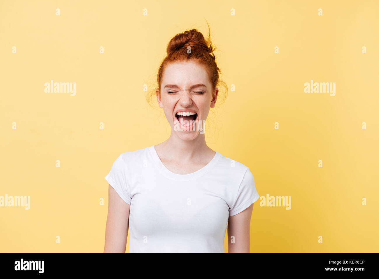Laughing ginger woman in t-shirt with closed eyes over yellow ...