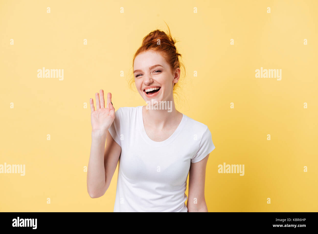 Laughing ginger woman wawing at the camera over yellow background Stock ...