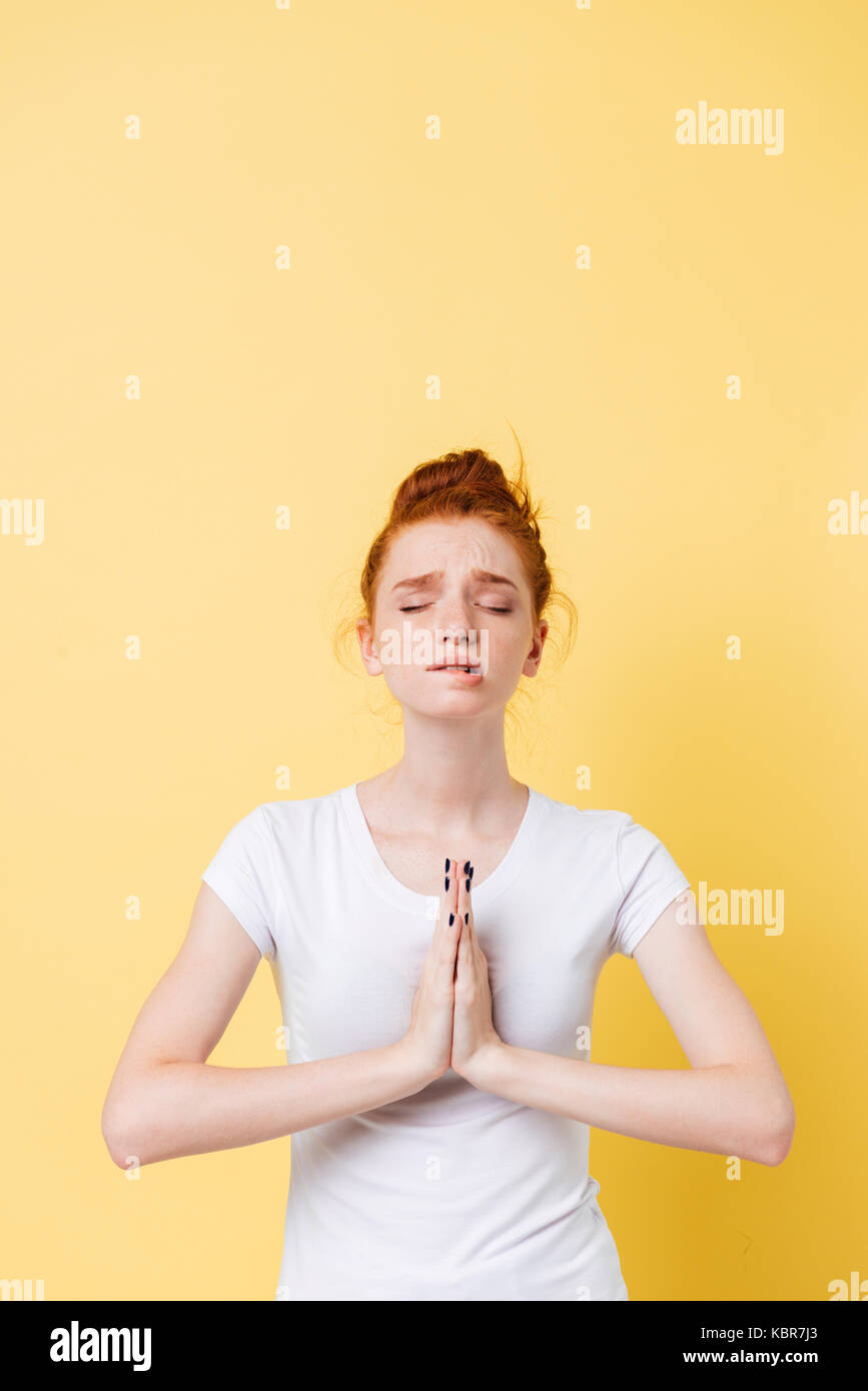 Vertical image of upset ginger woman in t-shirt praying with closed ...