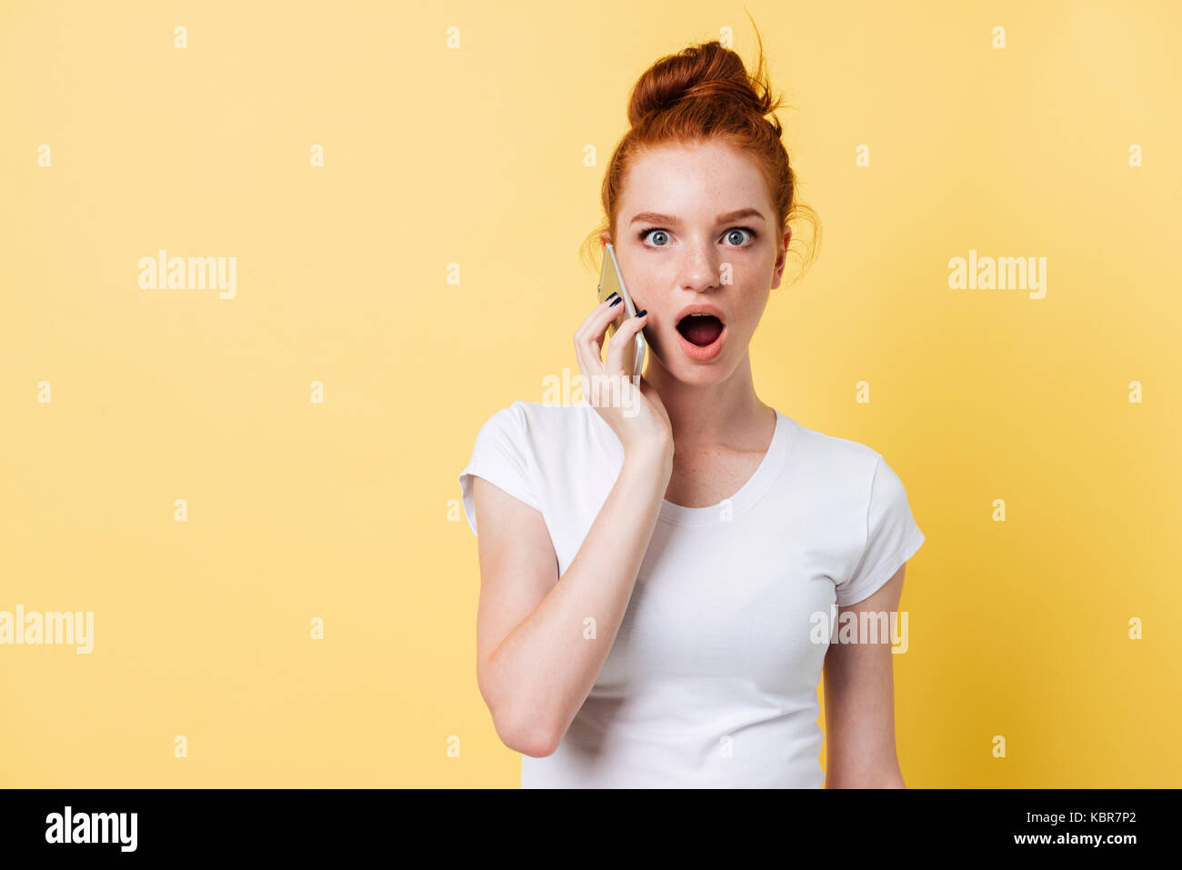 Shocked ginger woman in white t-shirt talking by the smartphone and ...