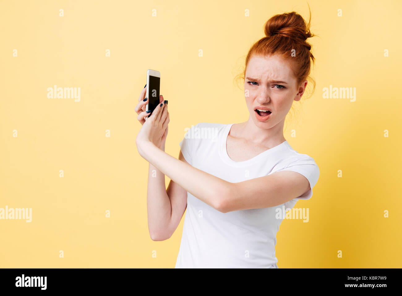 Surprised upset ginger woman in t-shirt covering her smartphone in ...